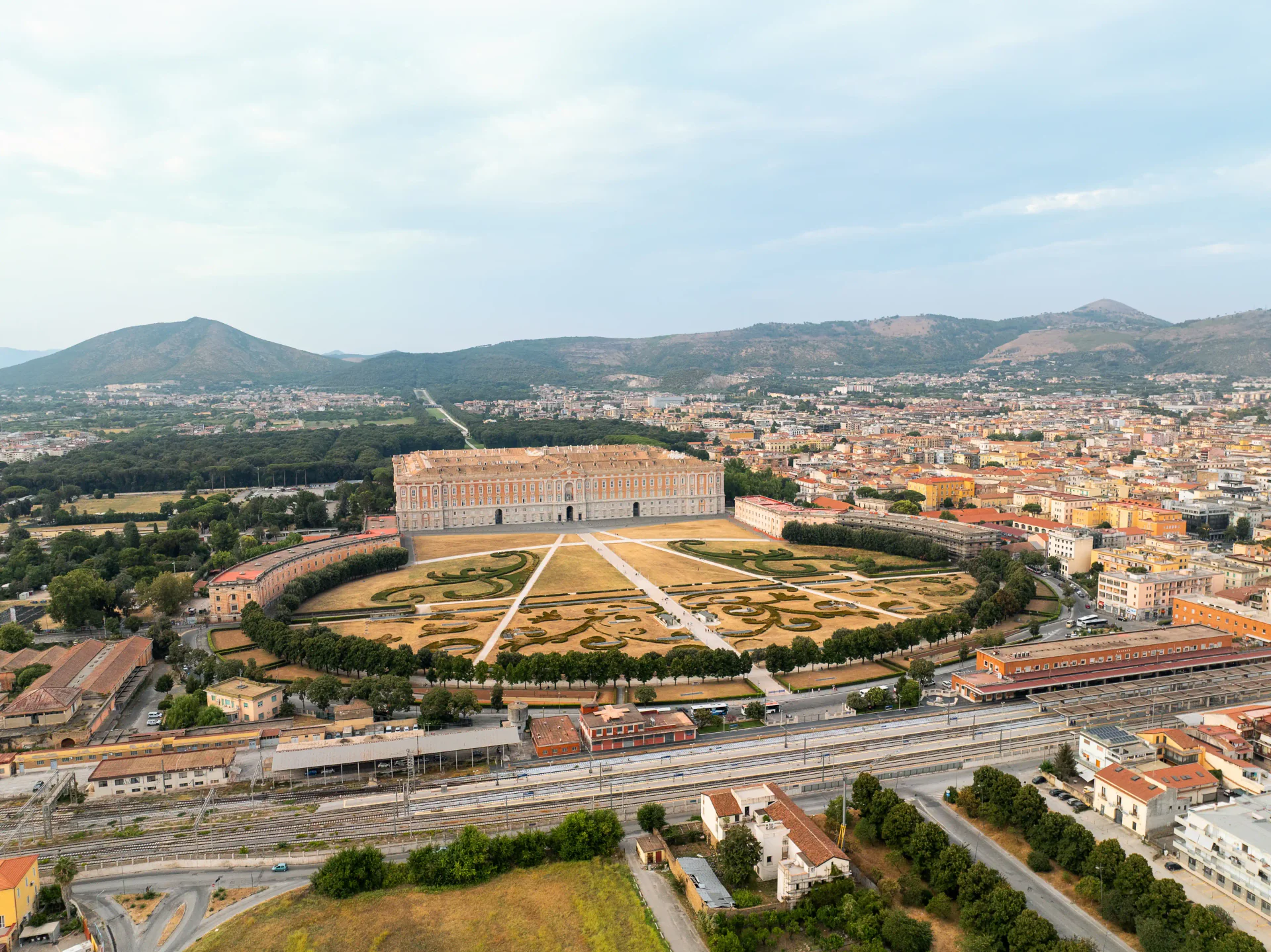Vista de Caserta La Reggia di Caserta, in Italia, patrimonio mondiale dell’UNESCO, circondata da giardini paesaggistici e aree verdi. La vista aerea mostra la sua grandiosa architettura, l’importanza storica e il suggestivo paesaggio circostante.