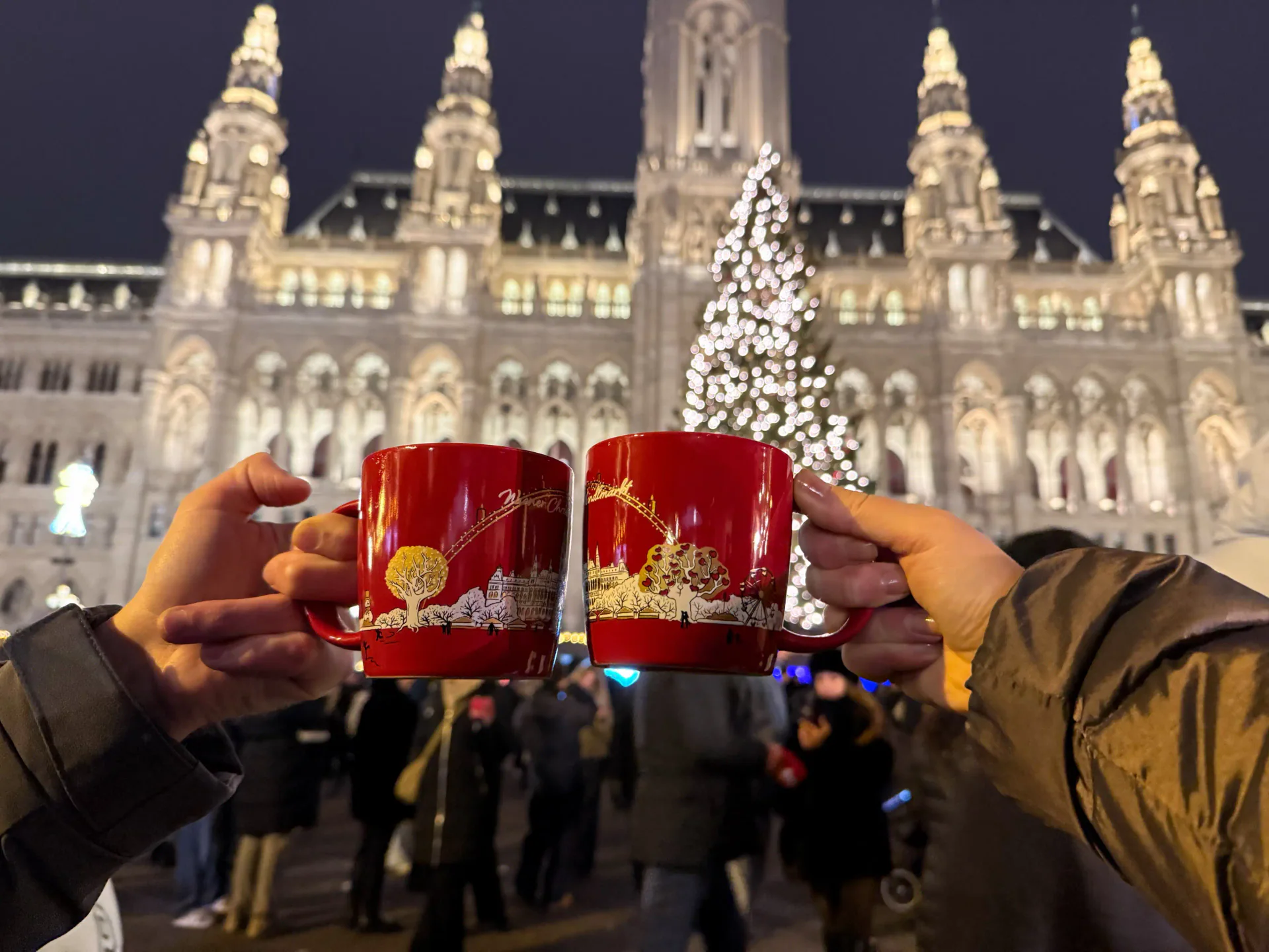 Vista di due tazze rosse festive con vin brulé, tenute tra le mani al famoso mercatino di Natale Christkindlmarkt in Rathausplatz, di notte.